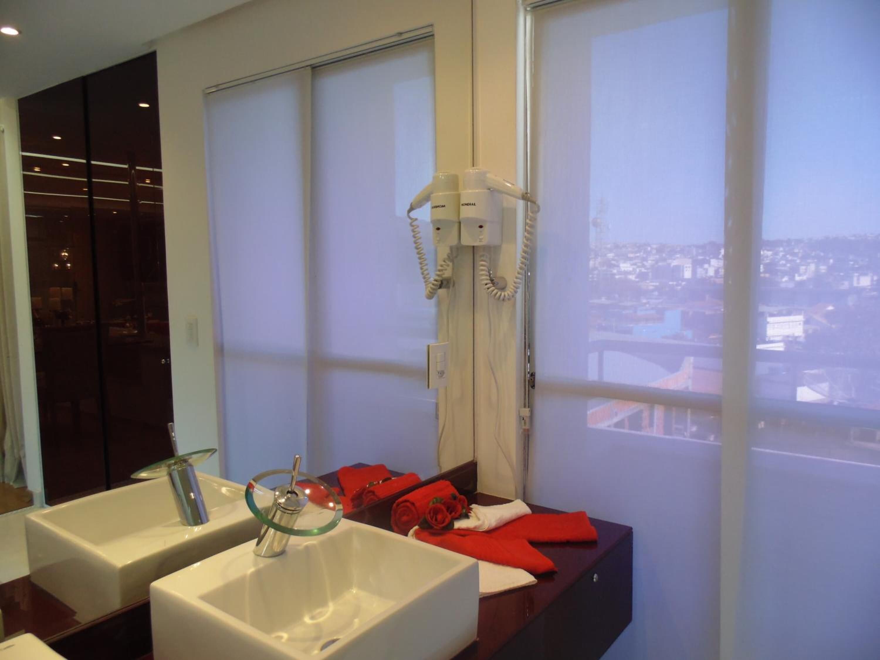 Uma casa de banho moderna com duas pias, cabine de duche com porta de vidro e vista para a cidade através de grandes janelas.