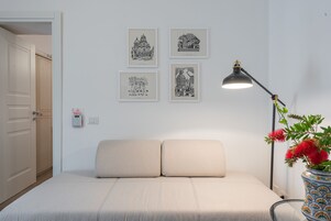 Um quarto bem organizado com uma cama, um abajur, um vaso com flores e quatro quadros na parede.