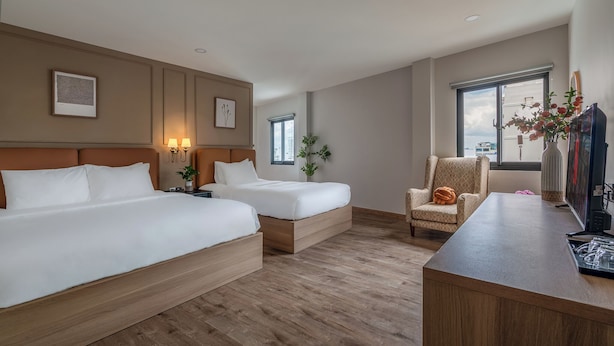 Quarto de hotel com duas camas, uma escrivaninha, uma cadeira, televisão e janela com vista.
