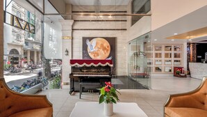 Um hall com um piano de cauda, uma pintura grande de um pássaro e uma lua, e vista para a rua.