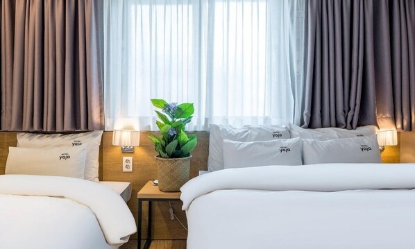 Quarto de hotel com duas camas, uma mesa de cabeceira, uma luminária e um vaso com planta.