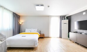 Quarto de hotel com cama, mesa de cabeceira, luminária, guarda-roupa, televisão e planta.