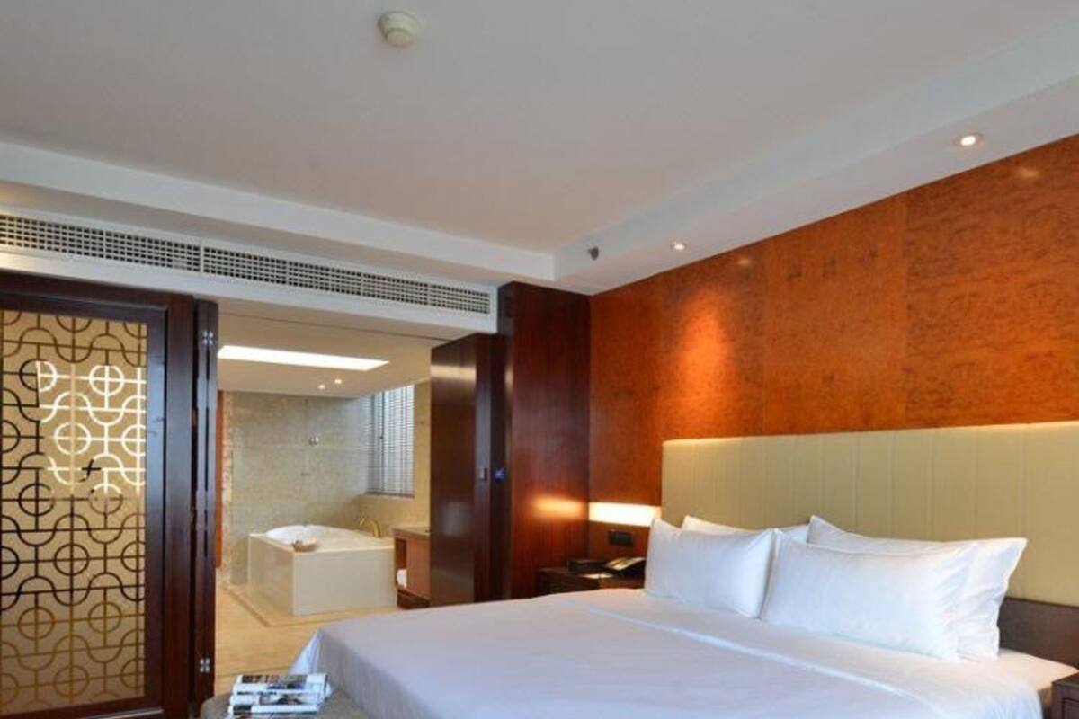 Quarto de hotel com uma cama grande, um banco, uma escrivaninha e um banheiro visível por uma porta aberta.