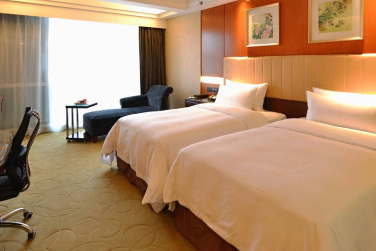 Quarto de hotel com duas camas, uma escrivaninha, uma cadeira e uma janela com cortinas.