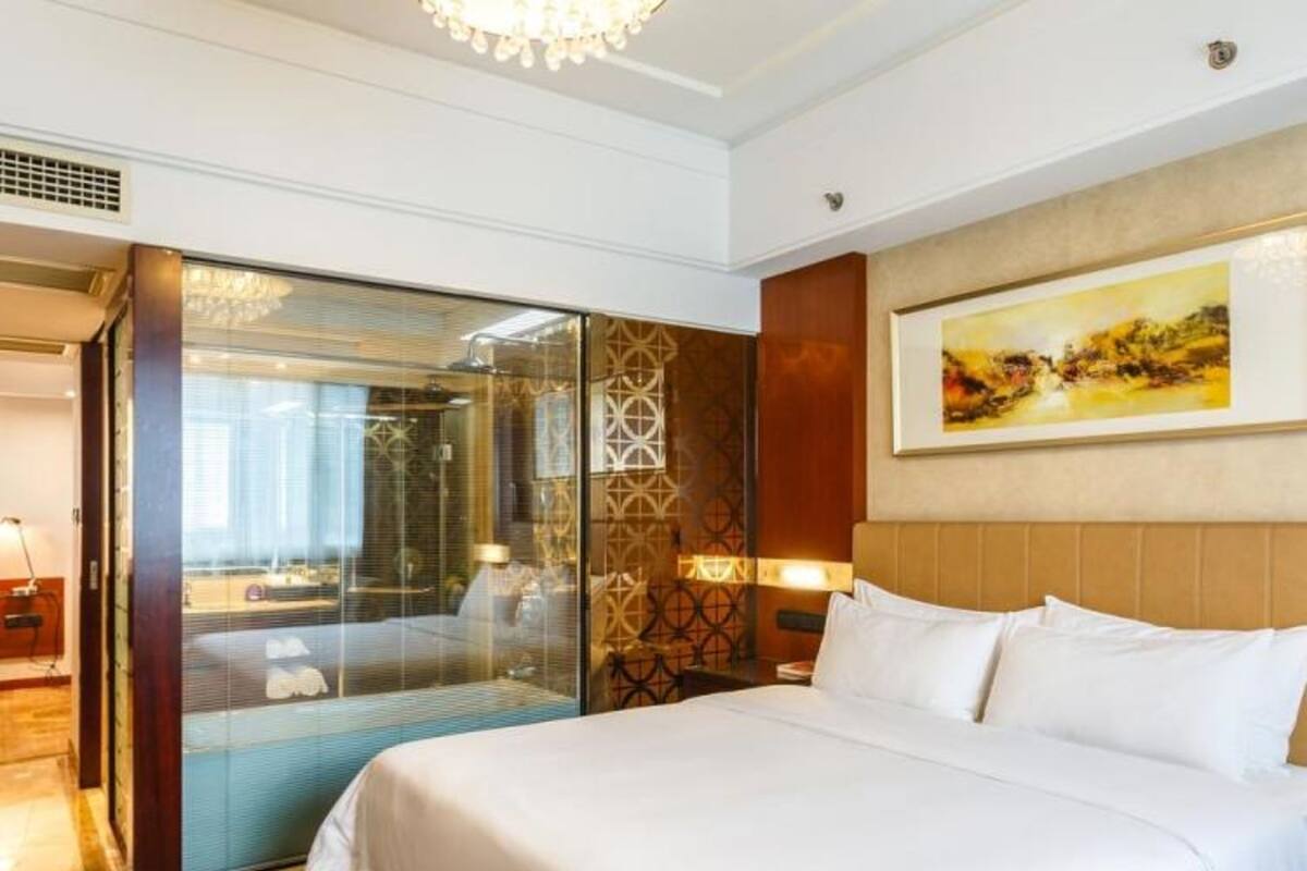 Quarto de hotel com cama grande, divisória de vidro e pintura na parede.