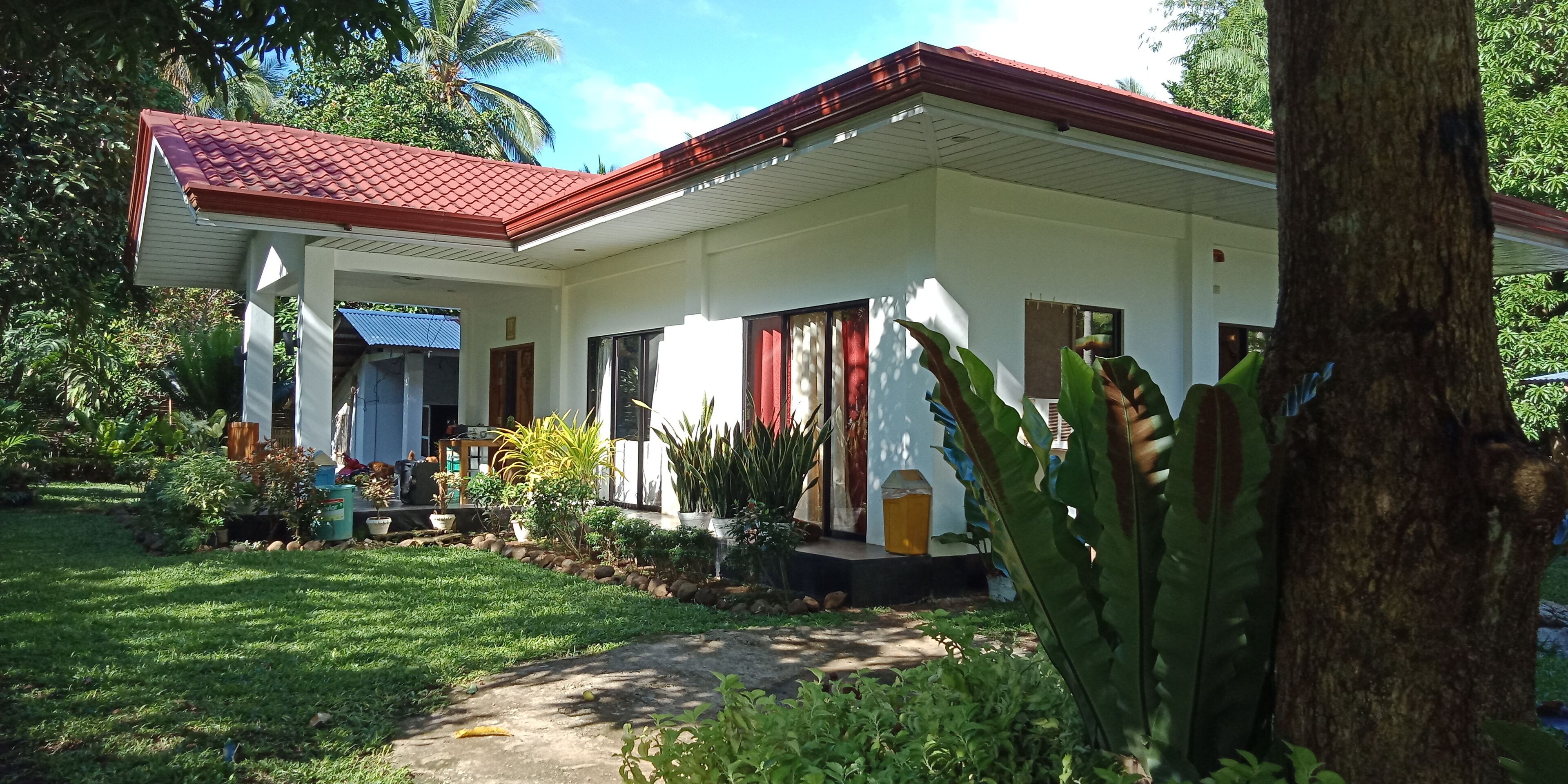 Uma casa de dois andares com telhado vermelho, paredes brancas e varanda coberta.