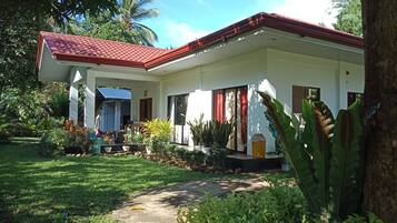 Uma casa de dois andares com telhado vermelho, paredes brancas e varanda coberta.