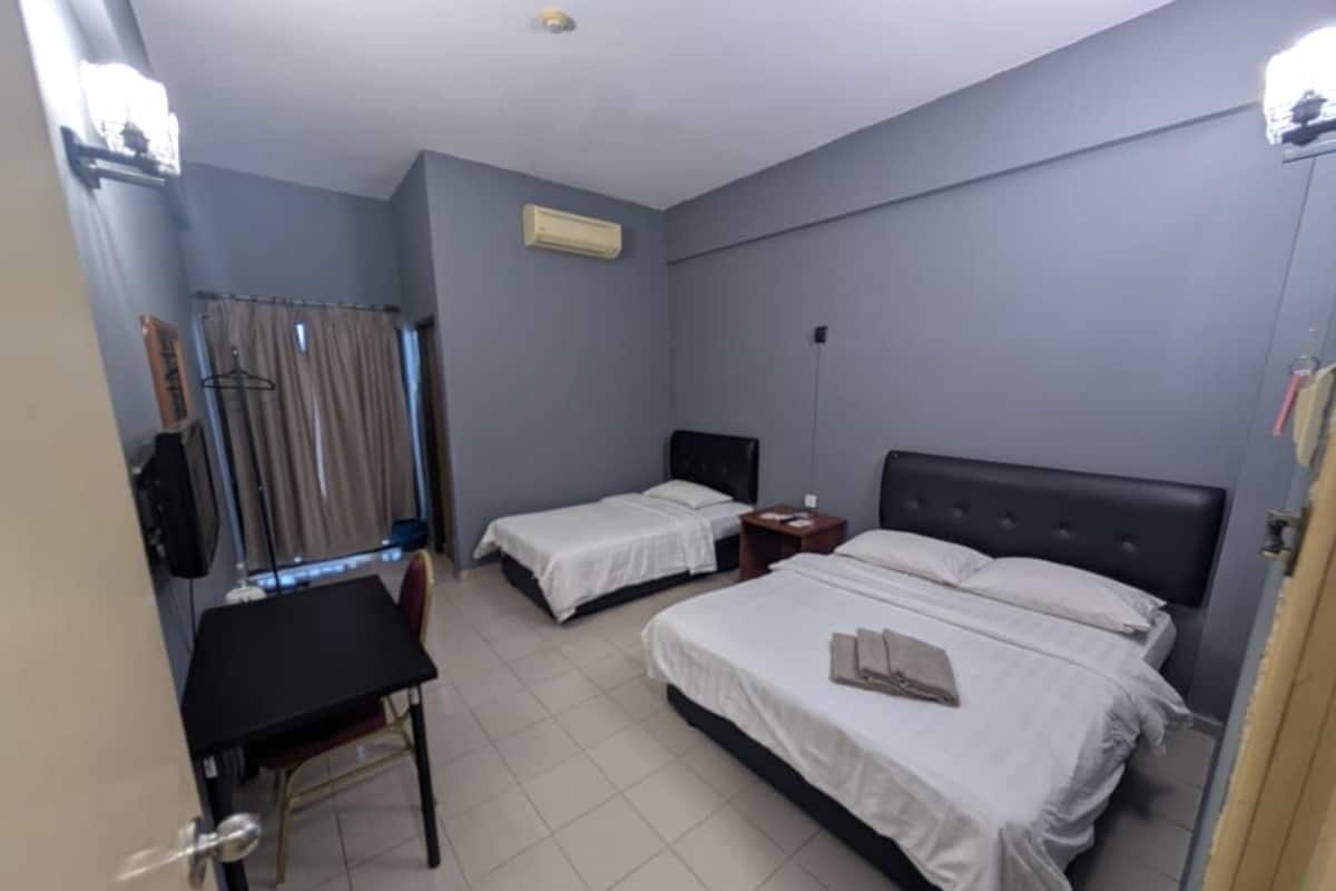 Quarto de hotel com duas camas de solteiro, uma pequena mesa e uma cadeira.