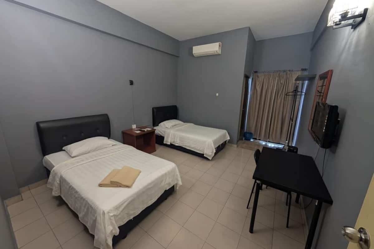 Quarto de hotel com duas camas, uma mesinha, ar condicionado e janela com cortinas.