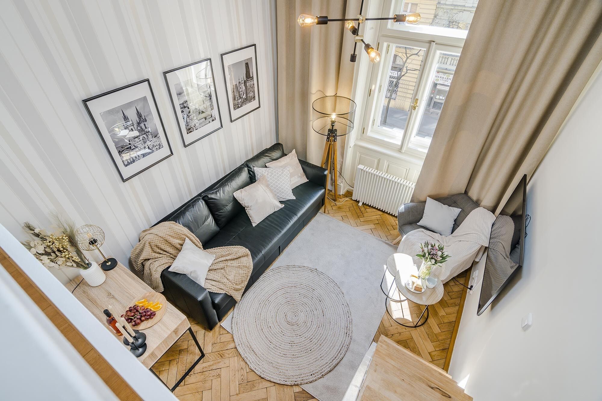 Uma sala de estar moderna com um sofá de couro preto, um tapete redondo de fibras naturais e uma área de jantar com mesa de madeira e um vaso de flores.