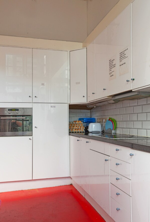 Uma cozinha com armários brancos, chão vermelho e painel de azulejos.