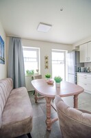 Uma cozinha moderna com armários brancos, uma geladeira de aço inoxidável e uma área de jantar com mesa e cadeiras rosa.