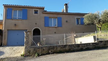 Uma casa de dois andares com base de pedra, garagem e cerca de metal.