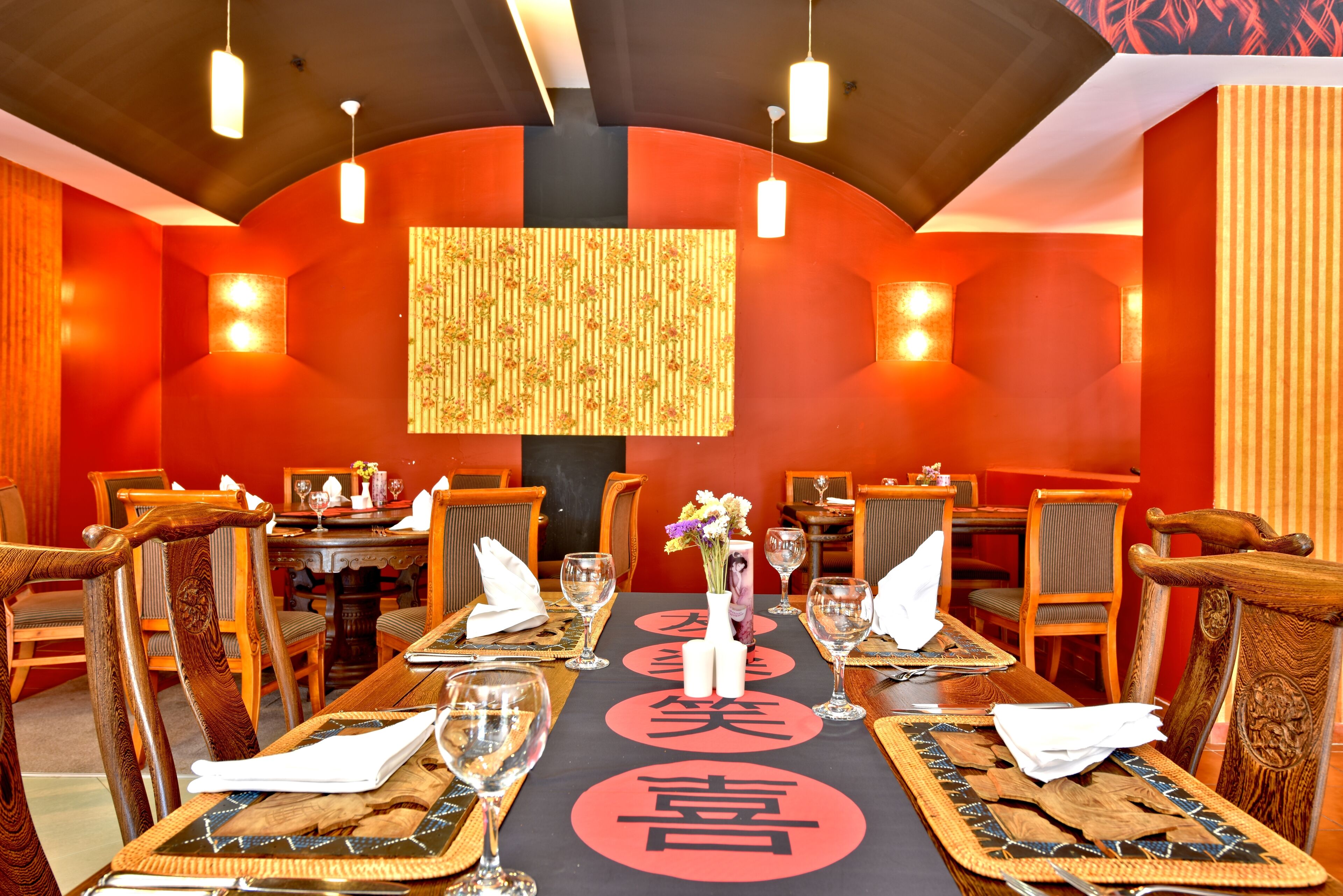 Um restaurante com mobiliário de madeira, um jogo americano preto com texto vermelho e preto, e um painel decorativo na parede.