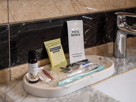 Uma pia de banheiro com artigos de higiene, incluindo uma garrafa de shampoo, um sabonete em barra e embalagem de lenços demaquilantes.