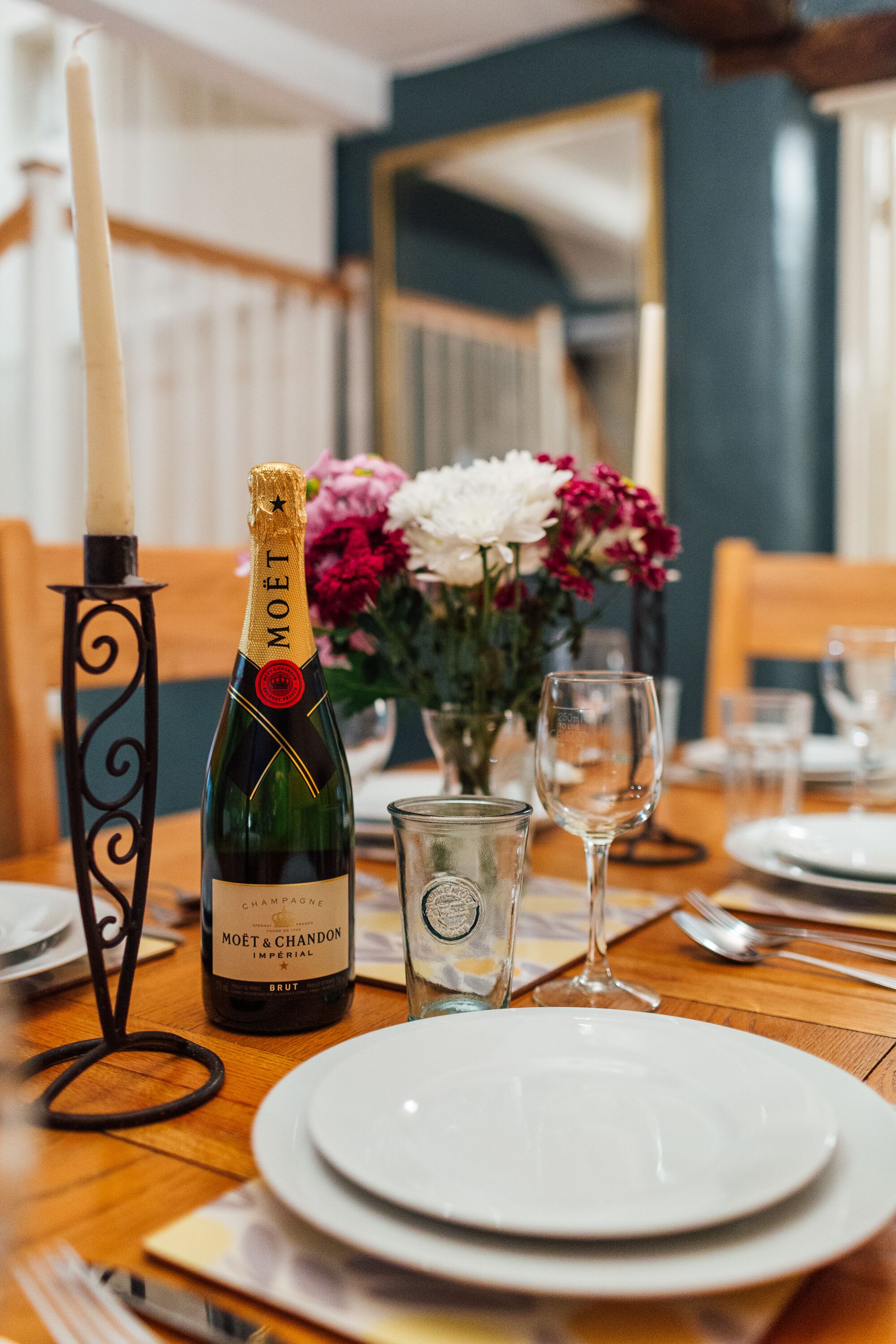 Uma mesa de jantar posta com uma garrafa de champanhe Moët & Chandon, uma taça e um vaso com flores.