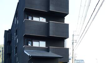Um edifício moderno de vários andares com fachada escura, uma placa indicando ser o Rikyuan Kyoto, e uma entrada com portão.