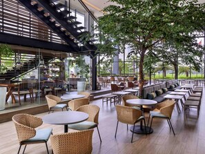 Um café moderno ao ar livre com móveis de vime, paredes de vidro e uma escadaria.