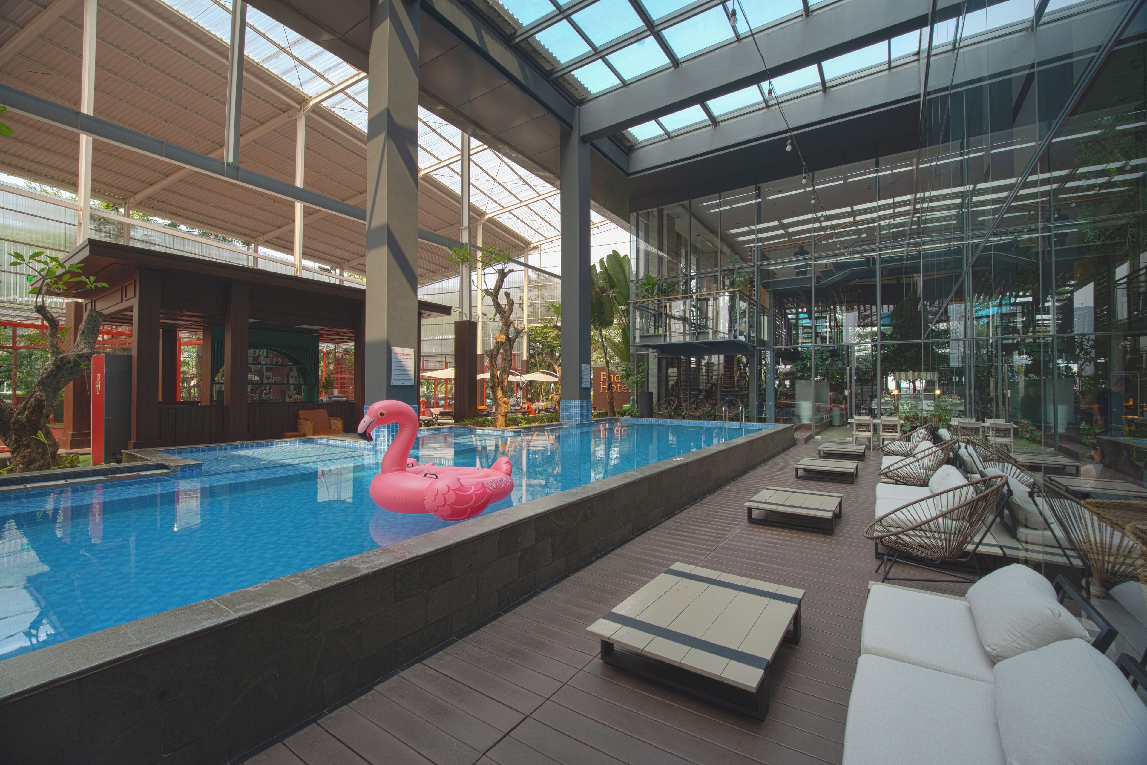 Piscina interna com flutuador em formato de flamingo rosa, cercada por cadeiras de descanso e uma área envidraçada com plantas.