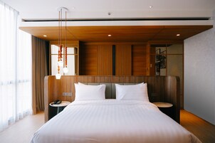 Quarto de hotel moderno com uma cama grande, cabeceira de madeira, mesas de cabeceira e um lustre.