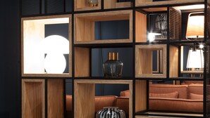 Um interior moderno com uma estante de metal preto com vários objetos, um sofá de couro marrom e uma mesa redonda.