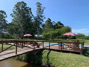 Um deck de madeira com piscina, rodeado por árvores e dois guarda-sóis vermelhos.