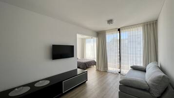 Uma sala de estar moderna com uma TV de tela plana na parede, um sofá cinza e piso de madeira.