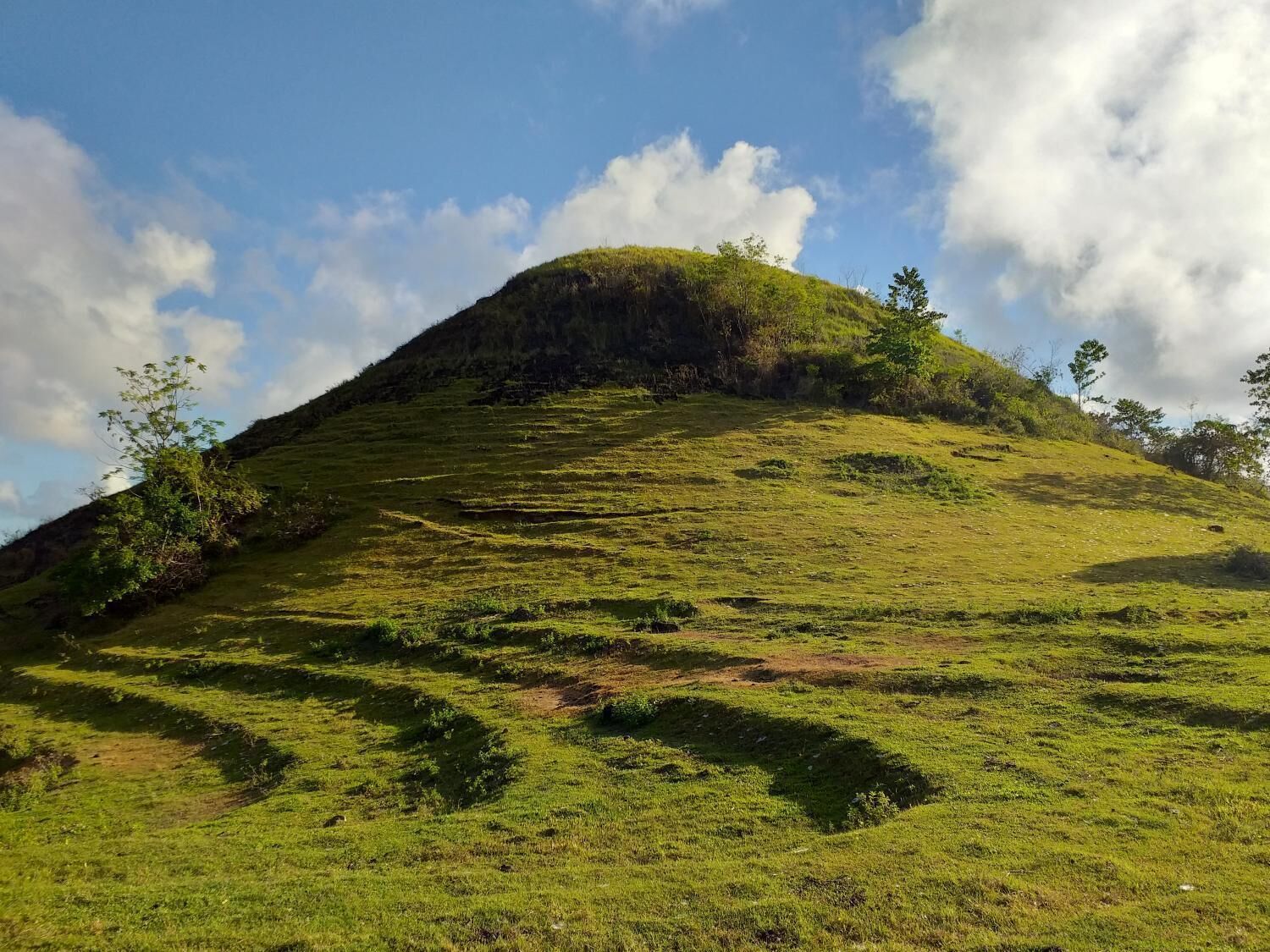 Uma colina gramada com um pequeno cume e vegetação escassa.