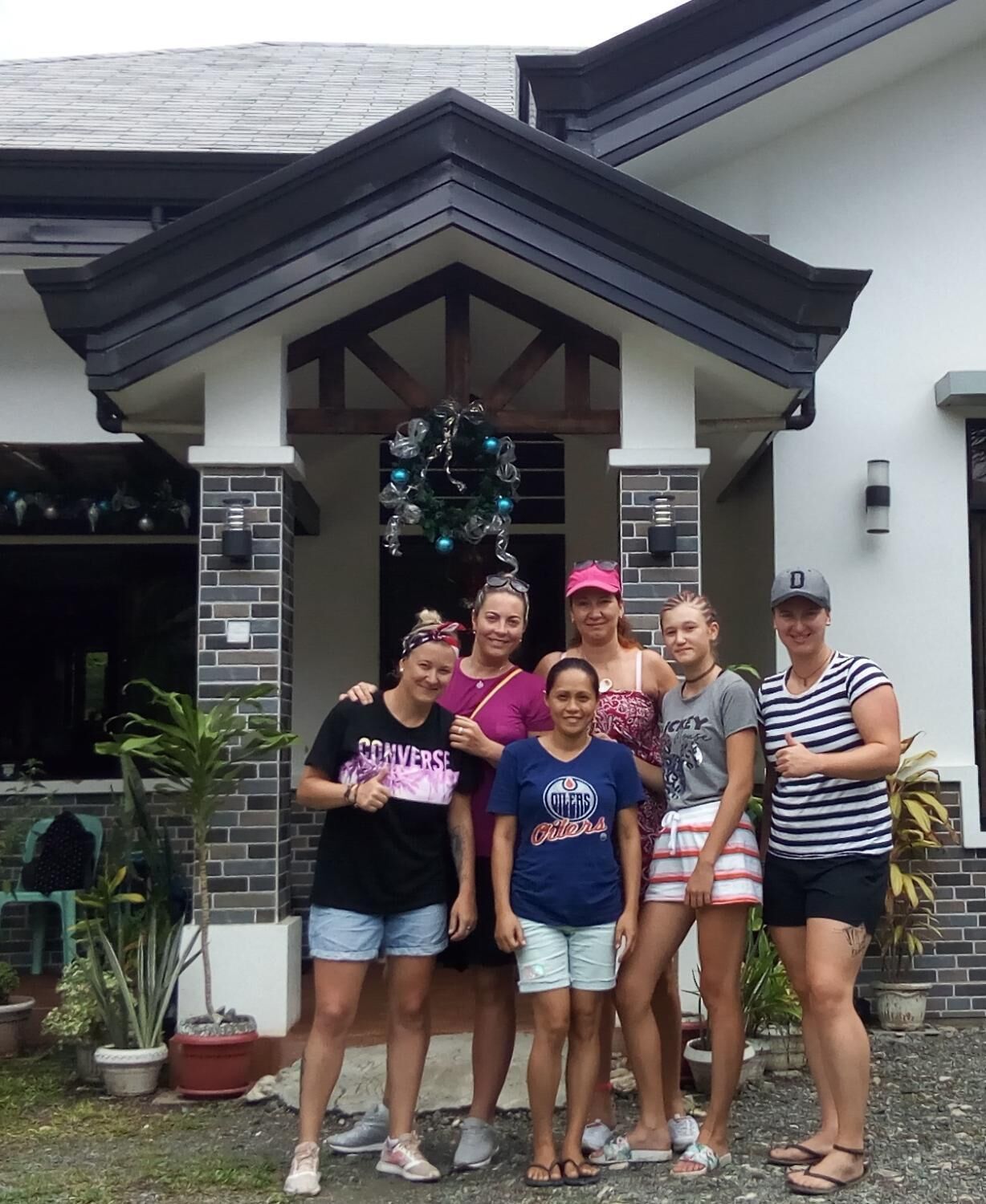 Um grupo de pessoas em frente a uma casa com fachada de tijolos, telhado preto e uma guirlanda decorativa.