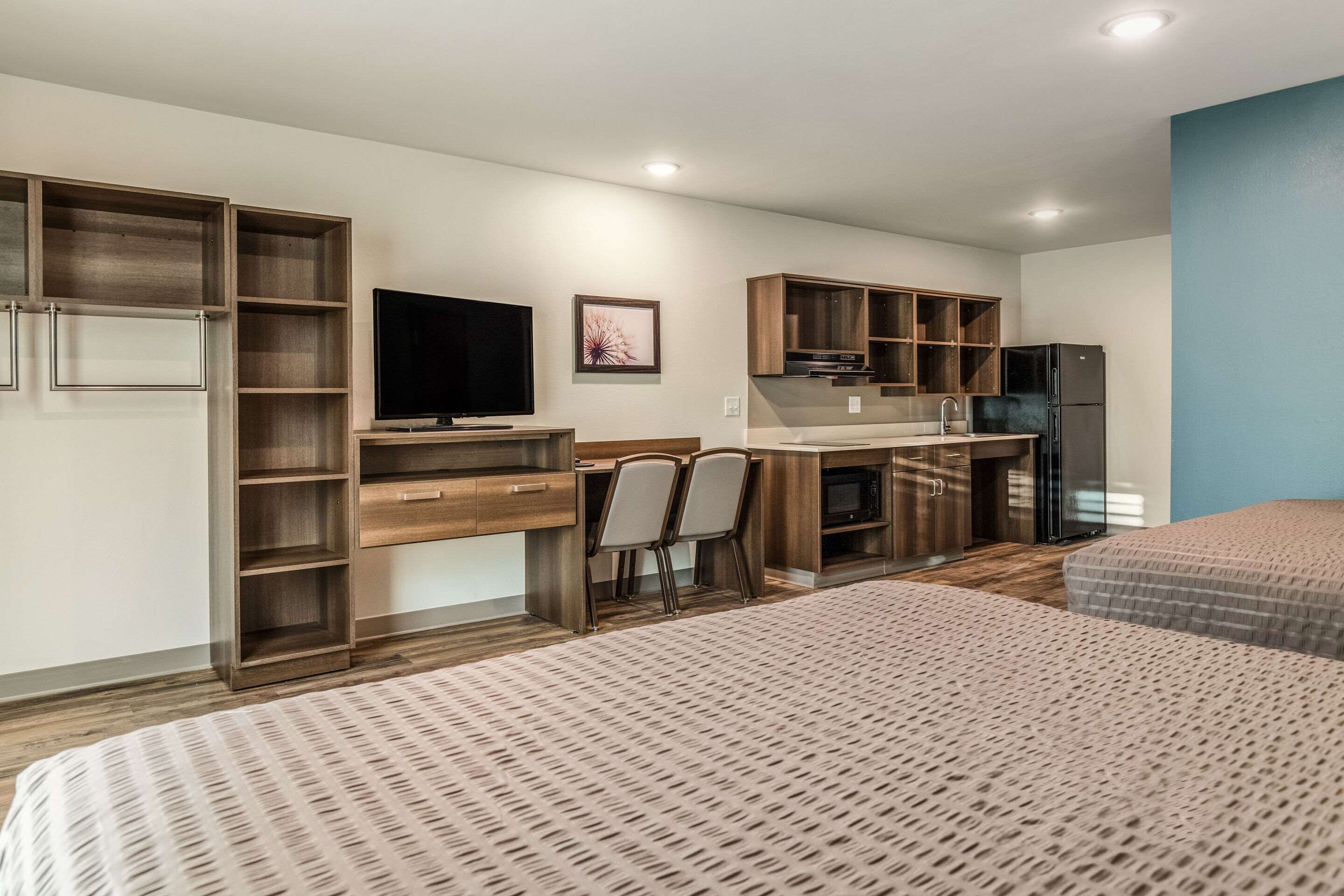 Quarto compacto com cama, escrivaninha, cadeira, televisão e cozinha compacta.