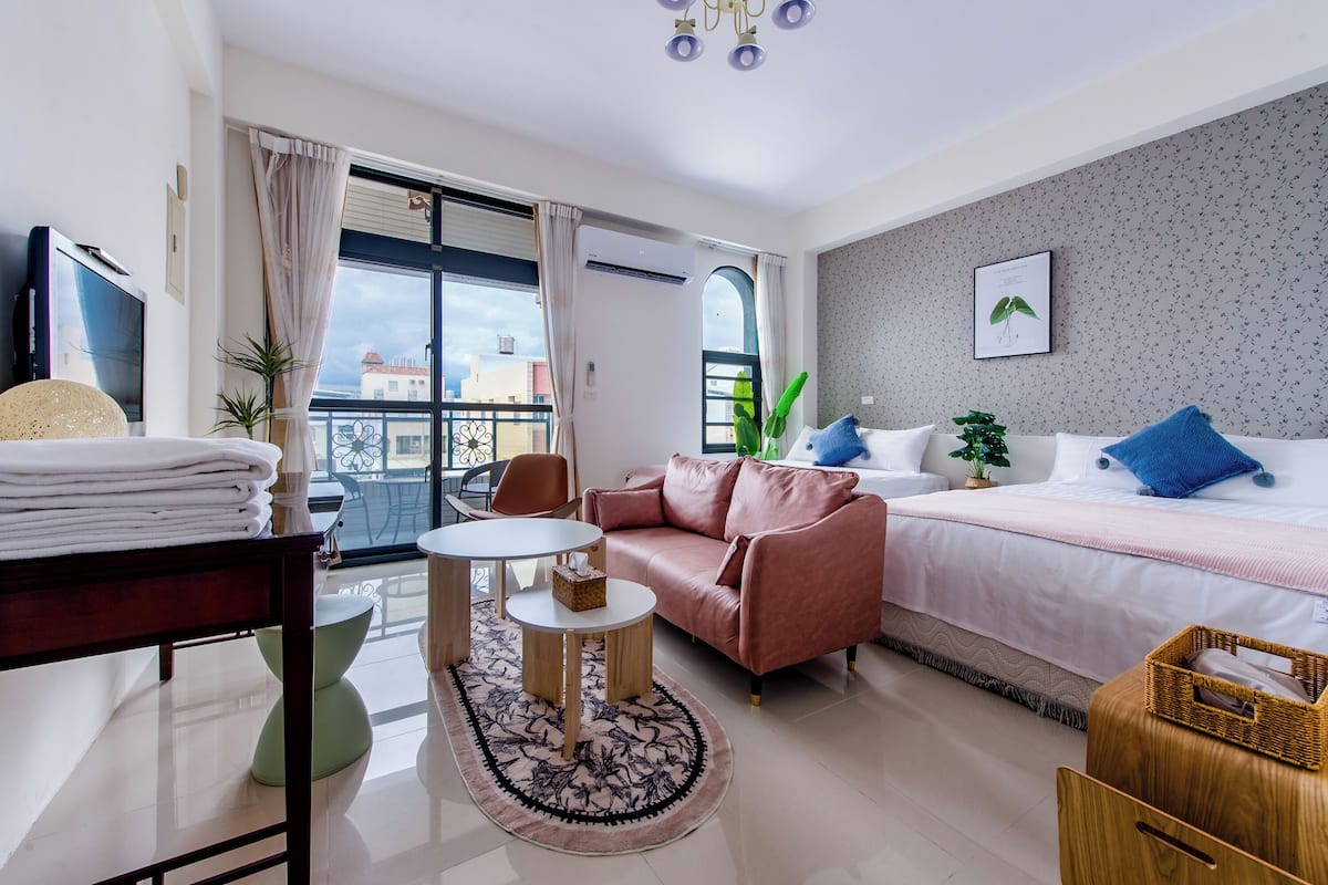 Quarto de hotel moderno com sofá, cama, mesa pequena e varanda com vista.