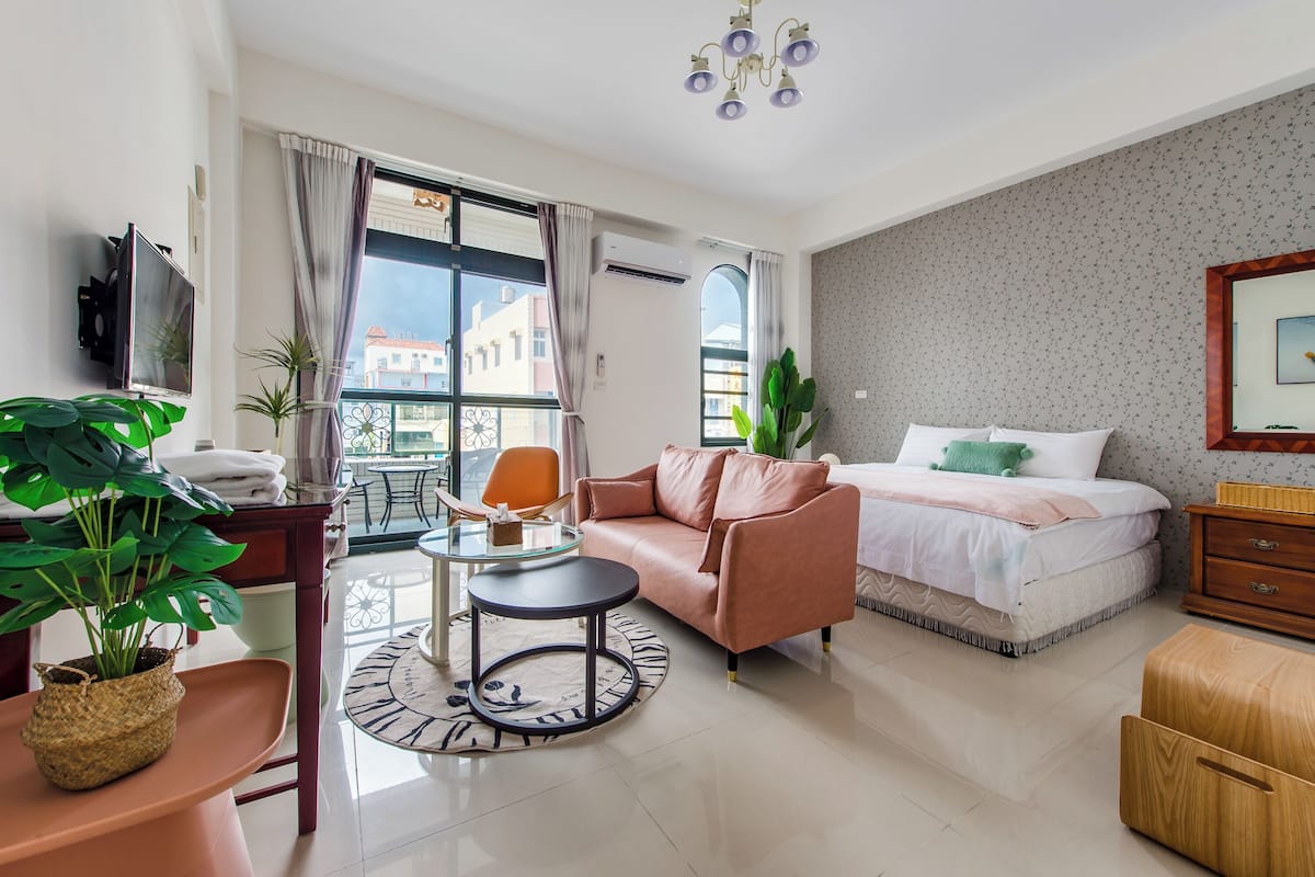 Quarto de hotel moderno com cama, sofá e área de refeições com mesa e cadeiras.