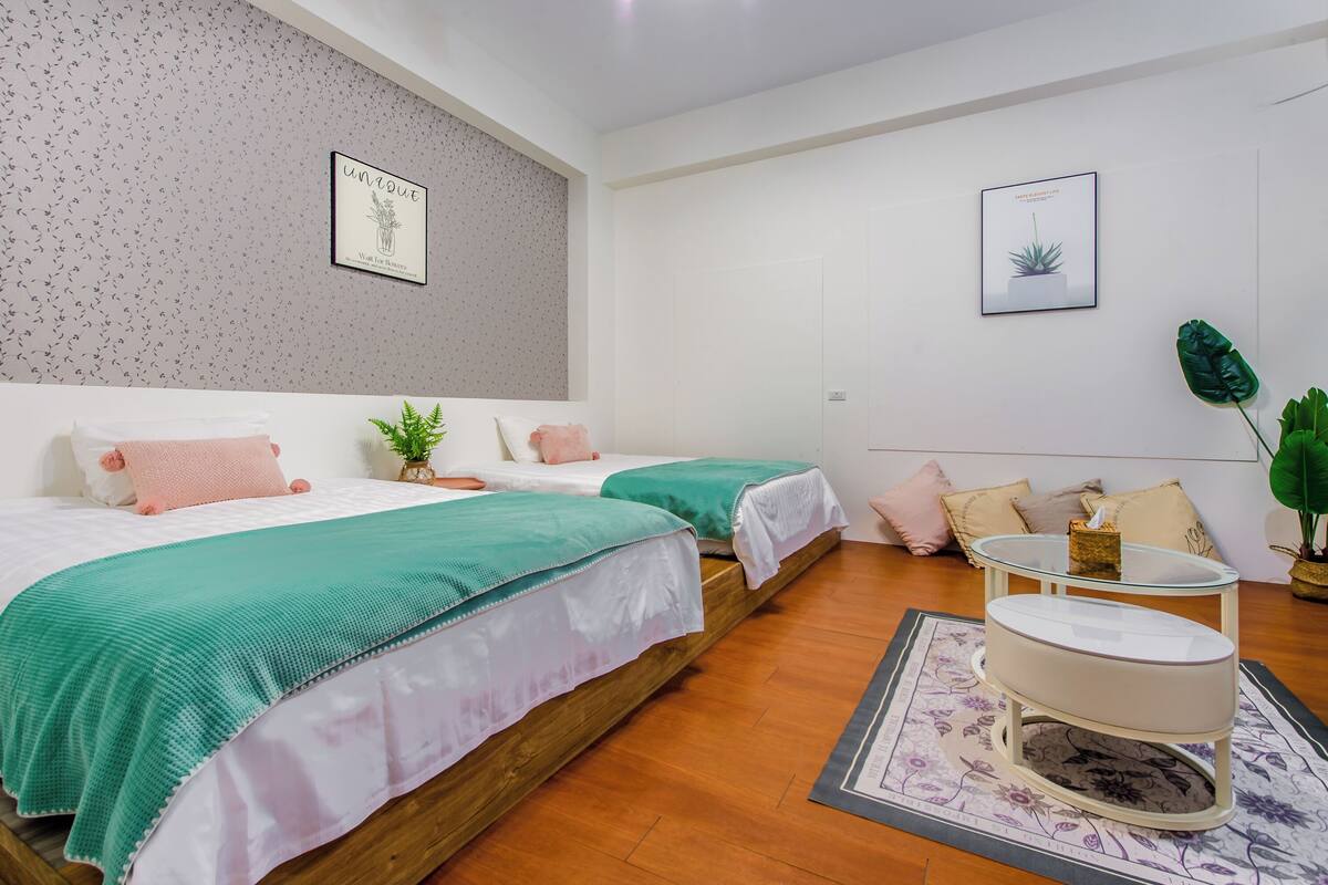 Quarto de hotel com duas camas, uma mesinha e um vaso de planta.