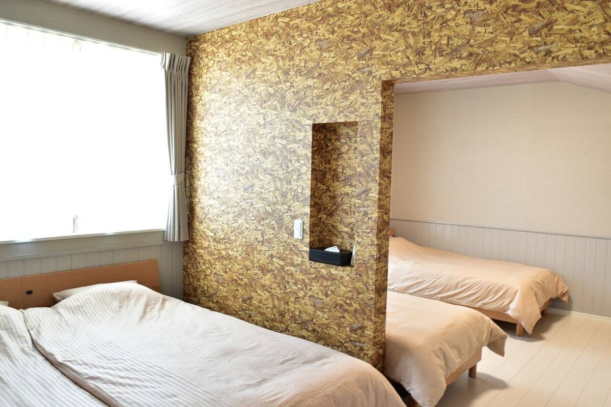Quarto com duas camas, janela com cortinas e parede com textura.