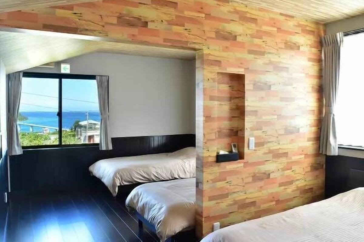 Quarto de hotel com duas camas, parede com padrão de tijolos, janela com vista e uma pequena prateleira.