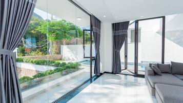 Sala de estar moderna com uma grande janela de vidro, um sofá cinzento e vista para um jardim bem cuidado.