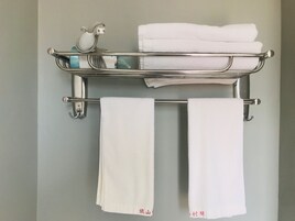 Um banheiro com um porta-toalhas com duas toalhas e uma toalha dobrada em uma prateleira.