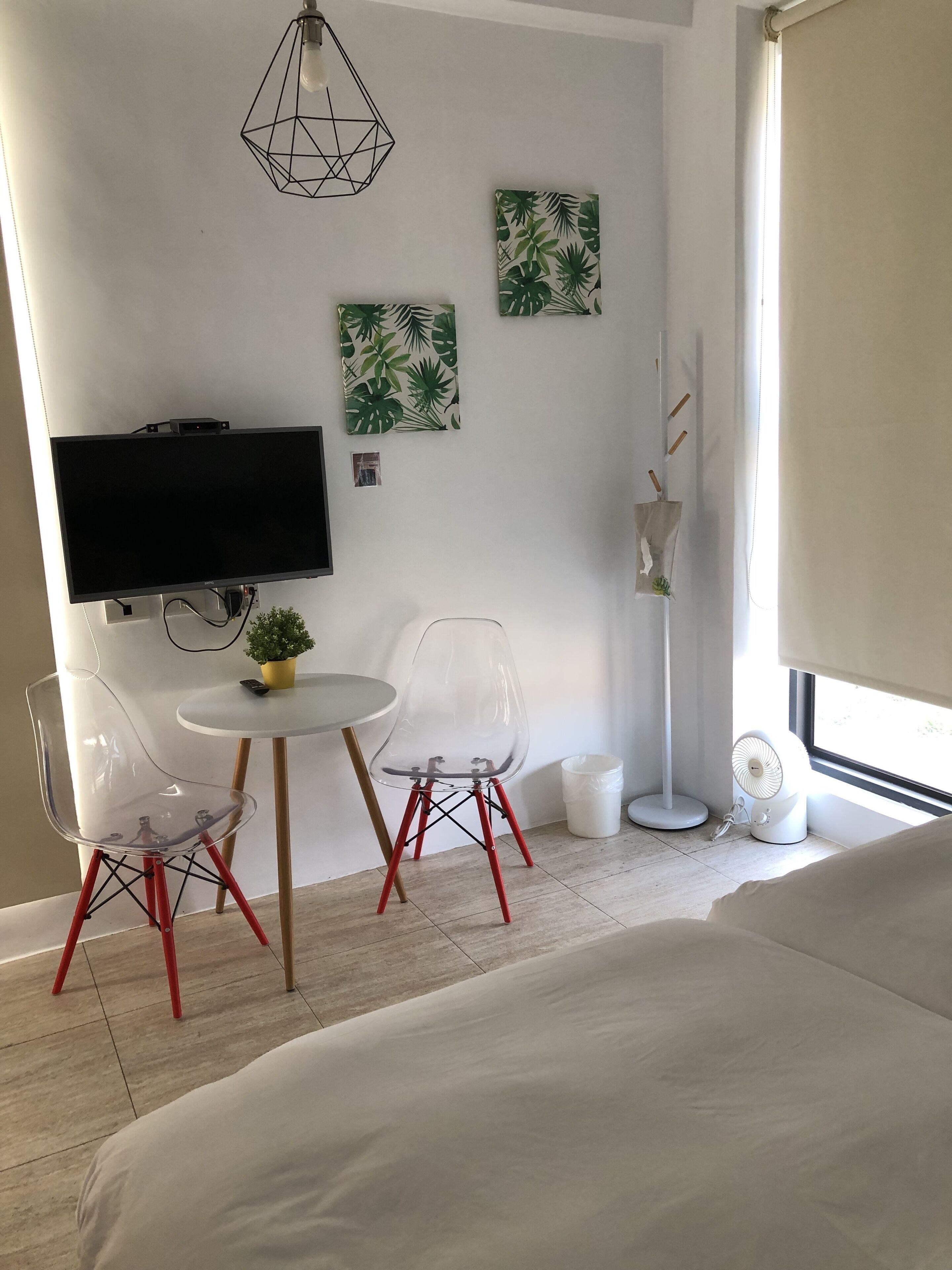 Quarto moderno com cama, televisão, uma mesinha com cadeiras e um vaso de planta.