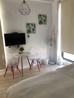 Quarto moderno com cama, televisão, uma mesinha com cadeiras e um vaso de planta.