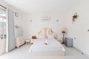 Quarto de hotel com cama grande, penteadeira, mesa de cabeceira, luminária e um pequeno frigorífico.
