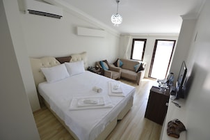 Quarto de hotel com uma cama grande, um sofá, uma escrivaninha com computador e uma televisão.