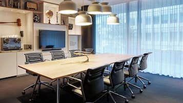 Uma sala de conferências com uma mesa comprida, cadeiras pretas, uma televisão e luminárias pendentes.
