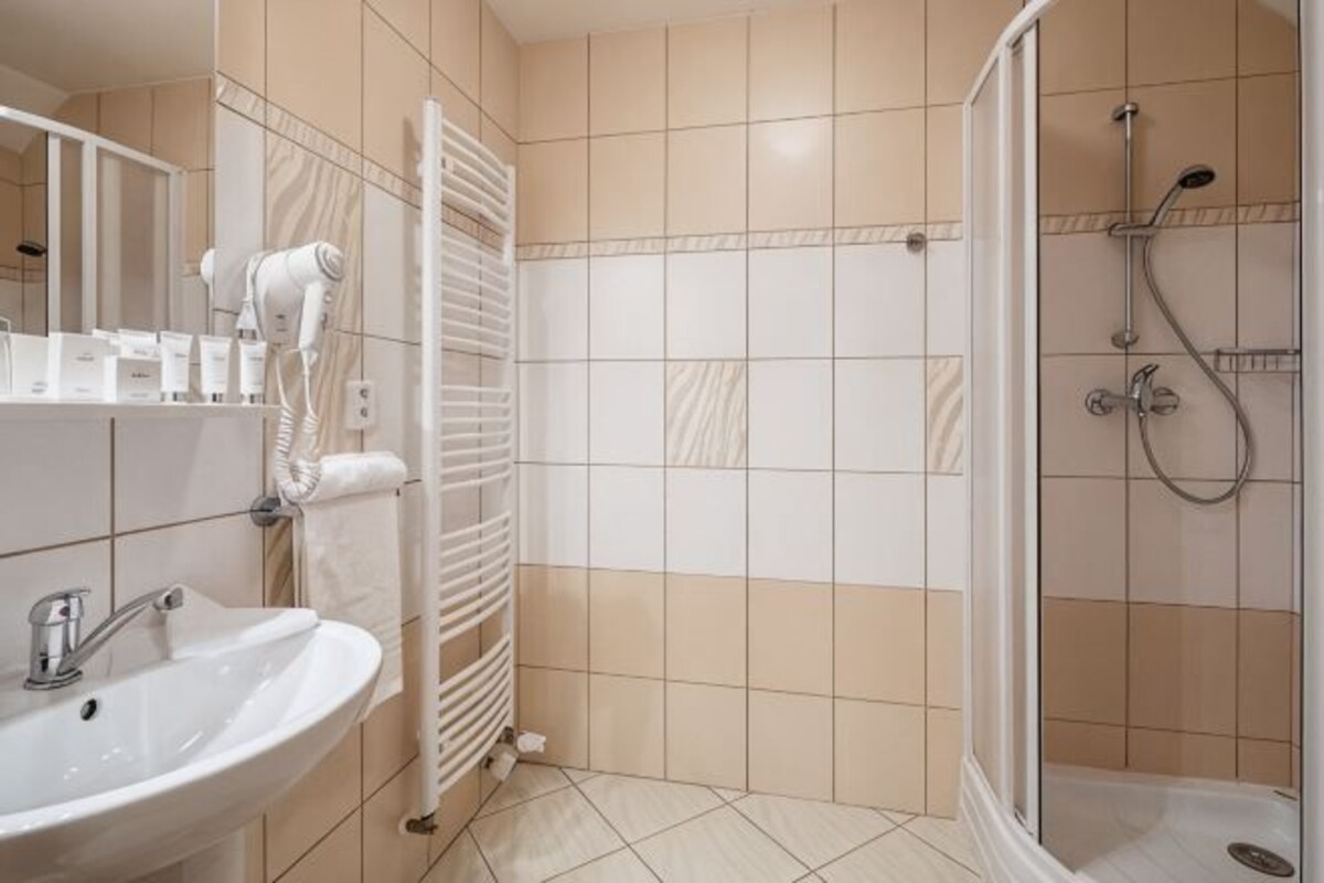 Casa de banho com lavatório, espelho, porta-toalhas e chuveiro.