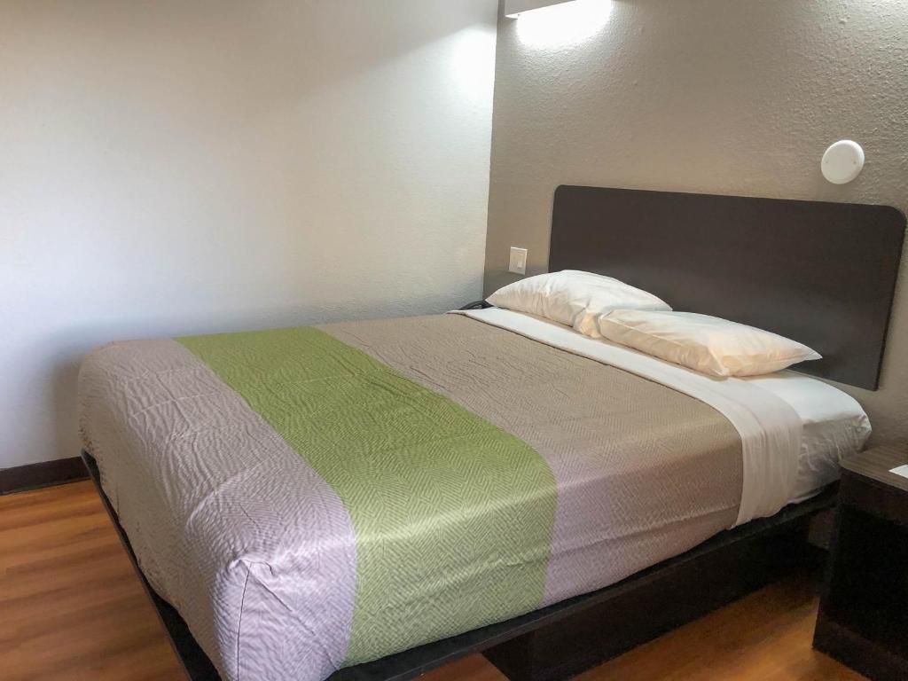 Uma cama de solteiro com cabeceira, mesa de cabeceira e luminária fixada na parede.