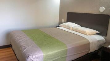 Uma cama de solteiro com cabeceira, mesa de cabeceira e luminária fixada na parede.