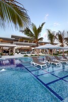 Uma área de piscina com espreguiçadeiras, guarda-sóis e um bar com área de estar ao ar livre.