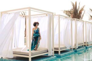 Área de piscina com estrutura tipo toldo, uma cama e uma palmeira ao fundo.