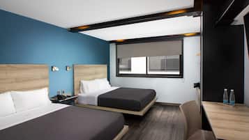 Quarto de hotel com duas camas, uma escrivaninha e uma janela.