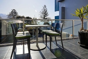 Uma varanda com mesa e cadeiras, um vaso de planta e vista para árvores e montanhas.
