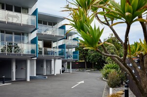 Um edifício moderno de vários andares, com varandas, área de estacionamento e jardim ajardinado.